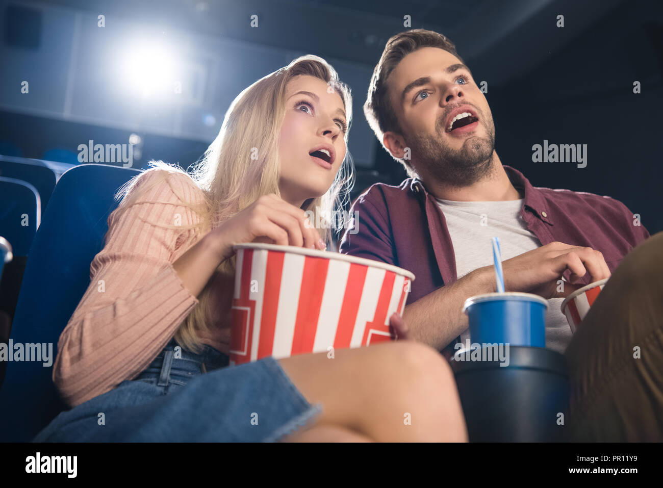 shocked couple with popcorn and soda drink watching film together in ...
