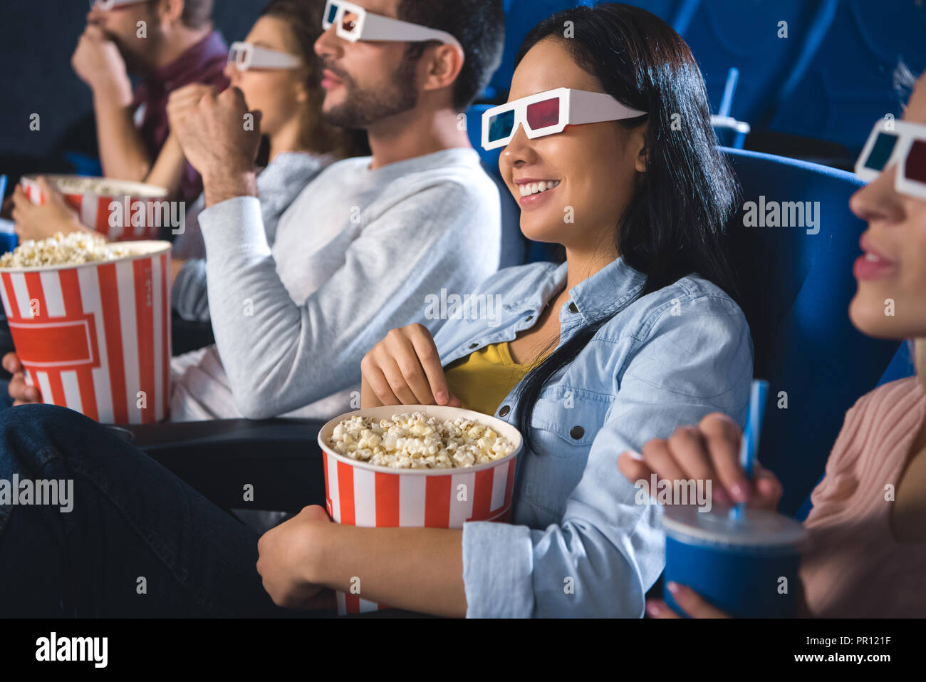 smiling multiethnic friends in 3d glasses with popcorn watching film together in movie theater ...