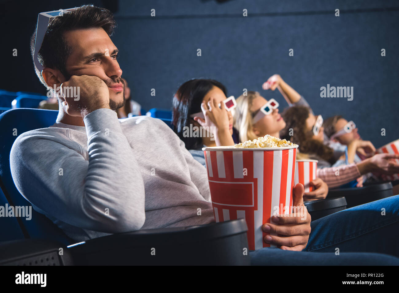 bored multiethnic friends with popcorn watching film together in movie ...