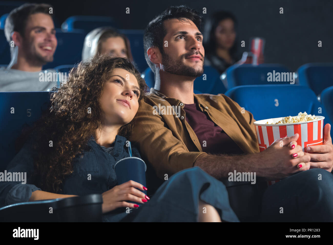 young couple with popcorn holding hands while watching movie together ...
