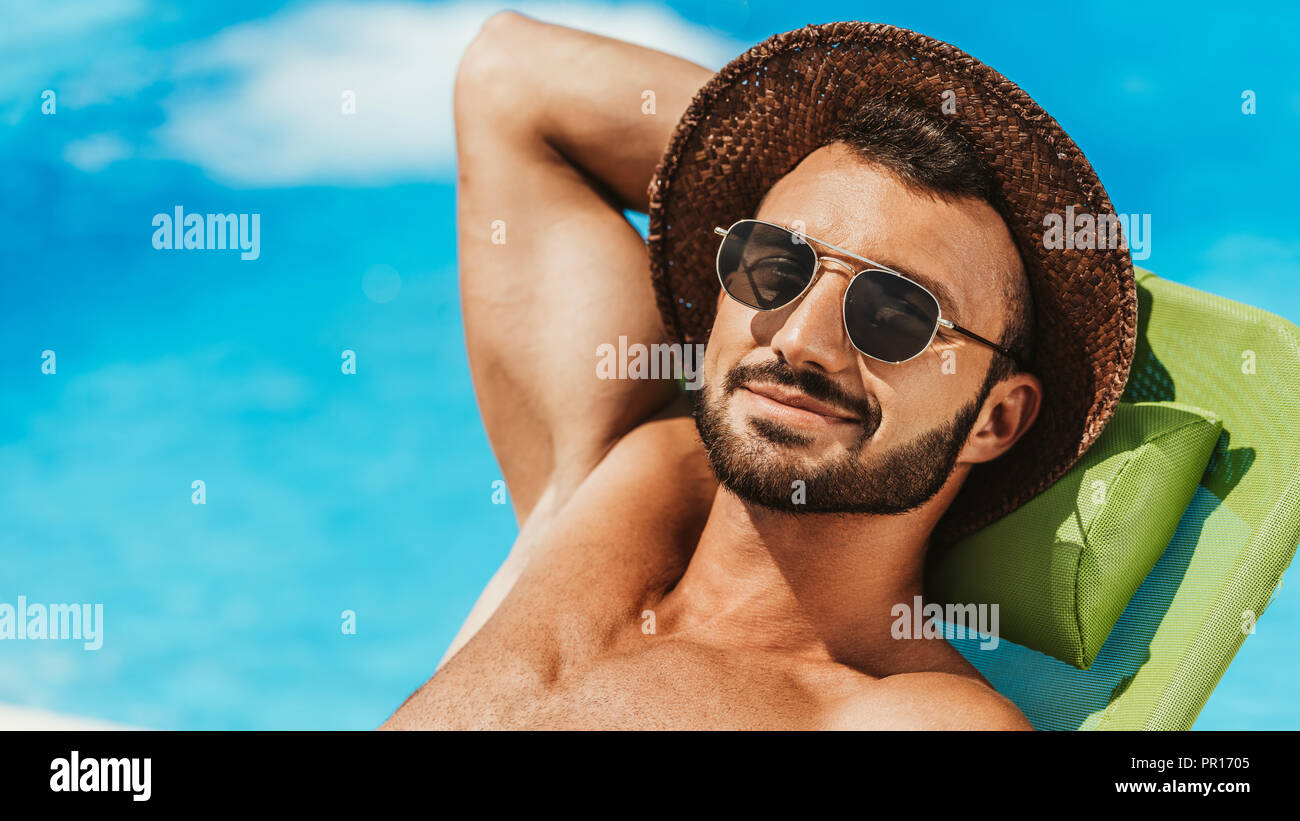 handsome man in sunglasses and straw hat sunbathing on sunbed at ...
