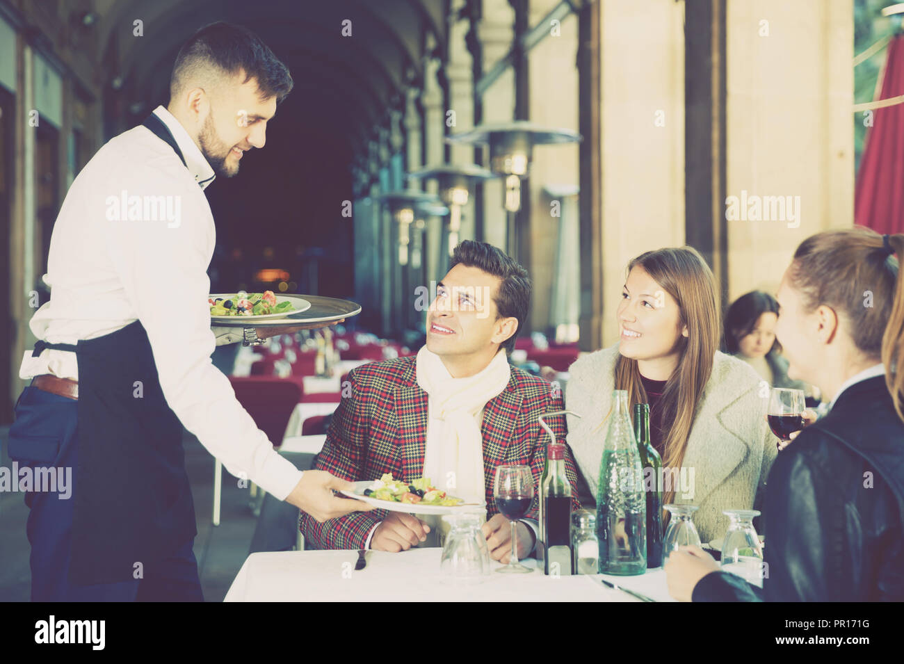 polite waiter serving guests at terrace cozy restaurant Stock Photo - Alamy