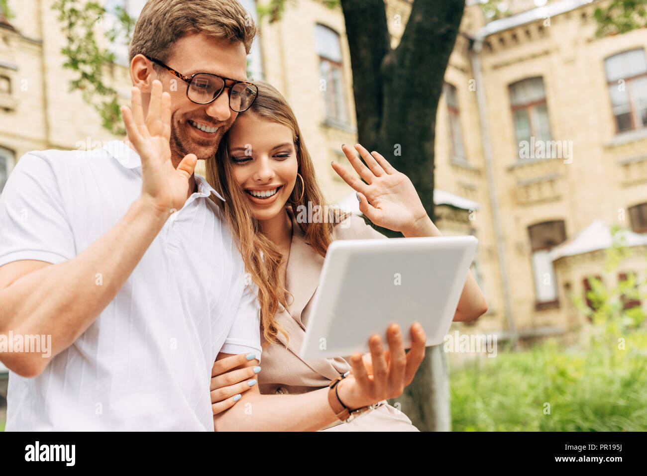 smiling young couple doing video call with tablet near old building ...