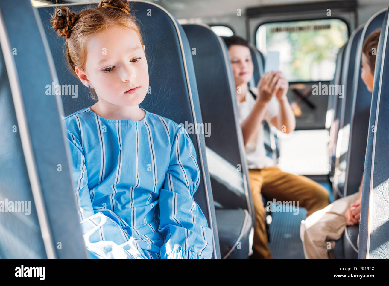 sad little schoolgirl sitting alone in school bus while her classmates ...