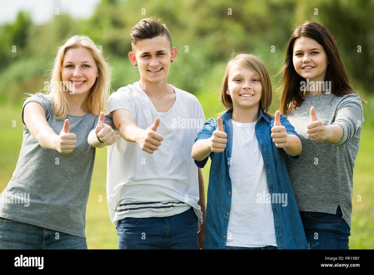 Portrait of four cheerful teenagers standing and holding thumbs up ...