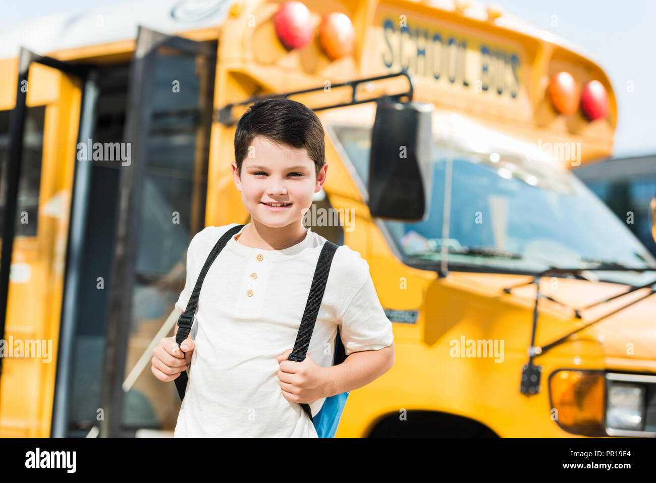 smiling little schoolboy with backpack standing in front of school bus ...