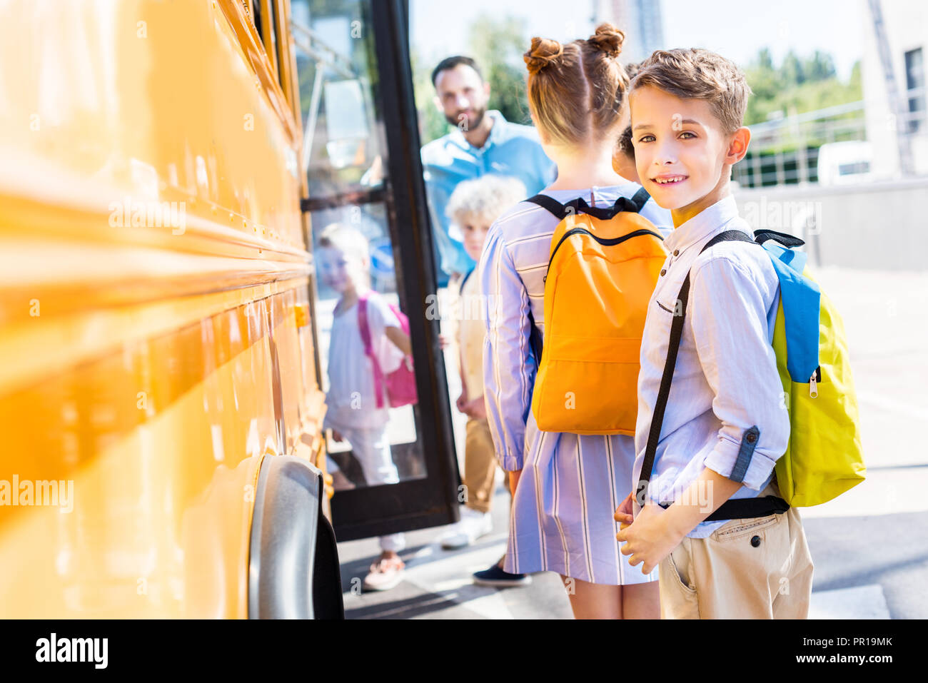 adorable schoolboy entering school bus with classmates while teacher ...