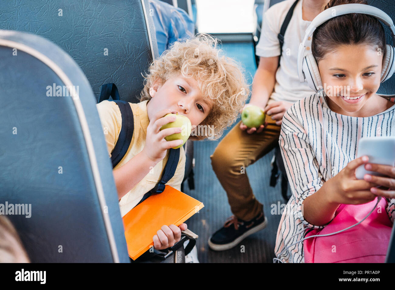 adorable little schoolboy eating apple while riding on school bus with ...
