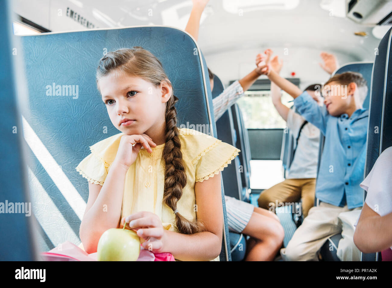 sad little schoolgirl riding on school bus while her classmates giving ...