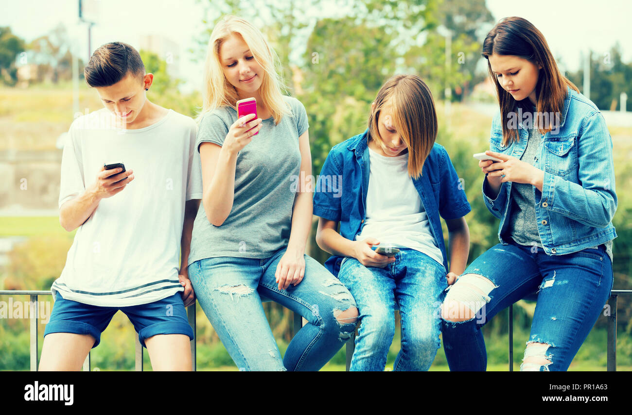 Two girls and two boys teenagers friends playing with mobile phones ...