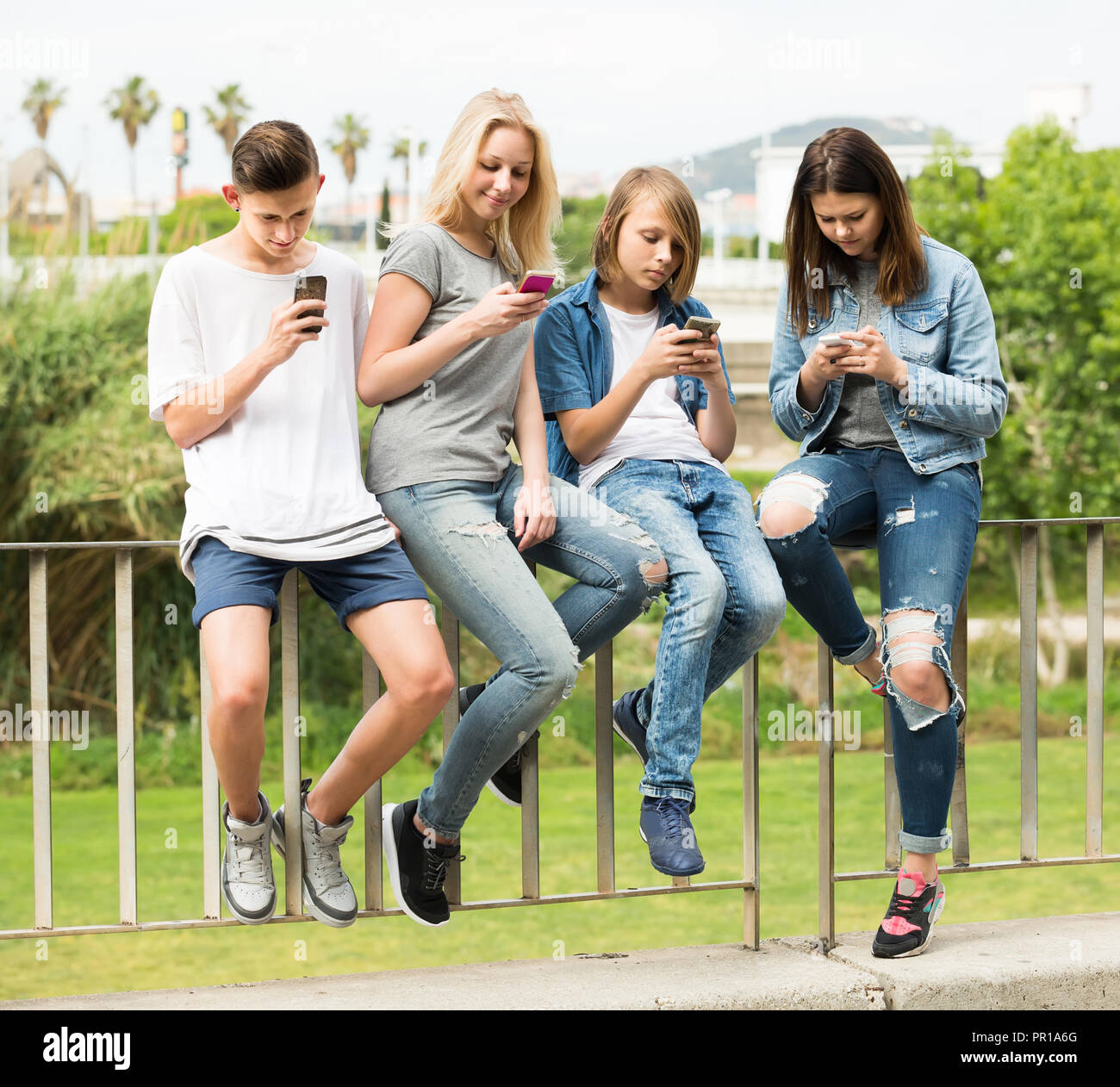 Portrait of four teenagers sitting with their mobile phones outdoors in ...