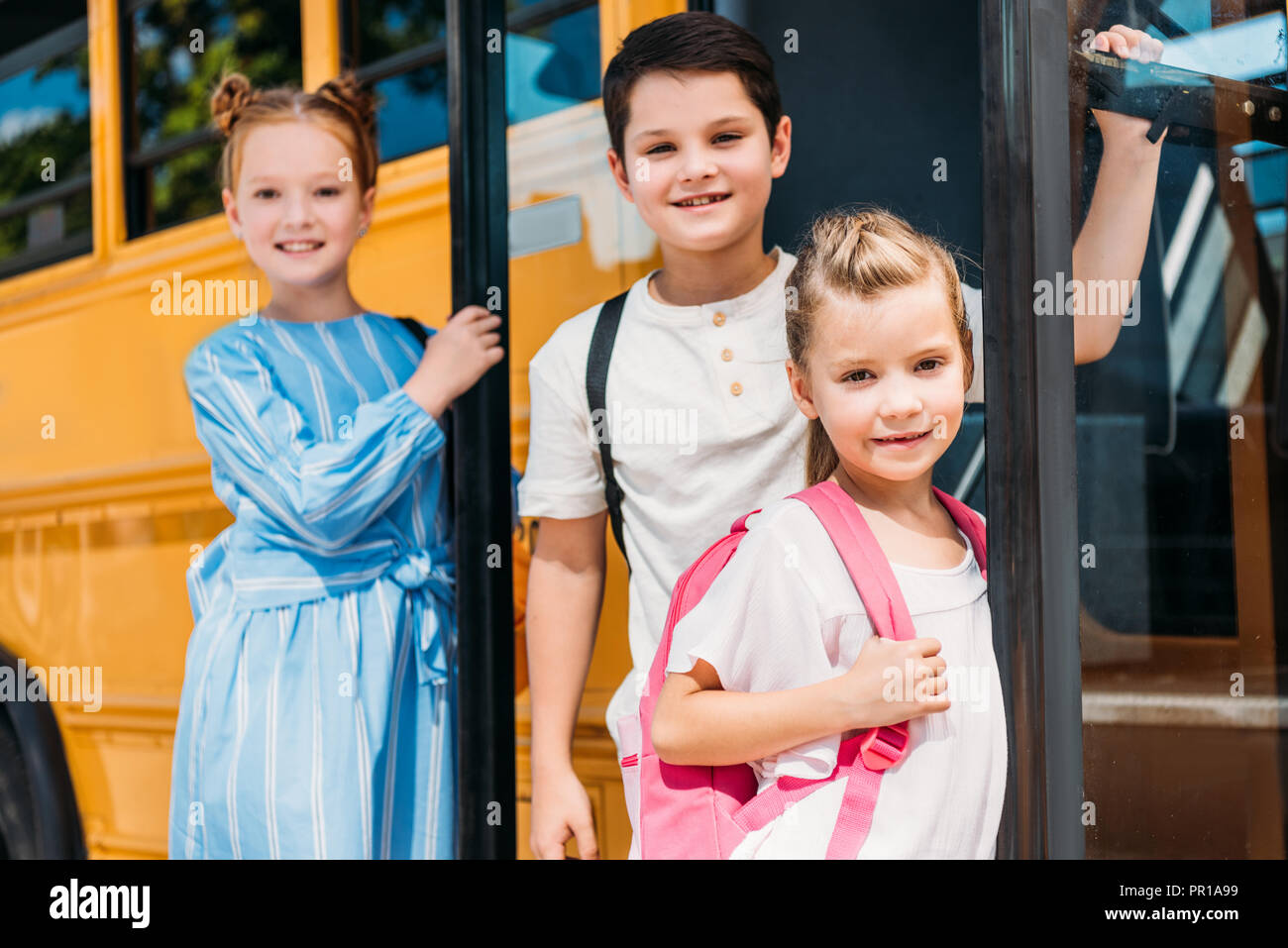 group of smiling pupils looking at camera near school bus Stock Photo ...