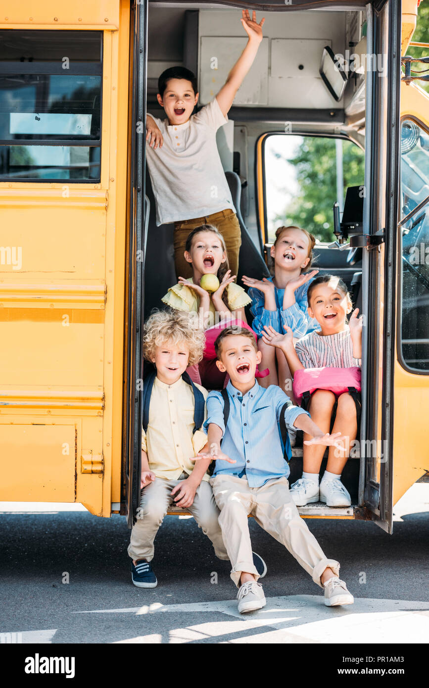 group of adorable schoolchildren sitting on stairs of school bus and ...