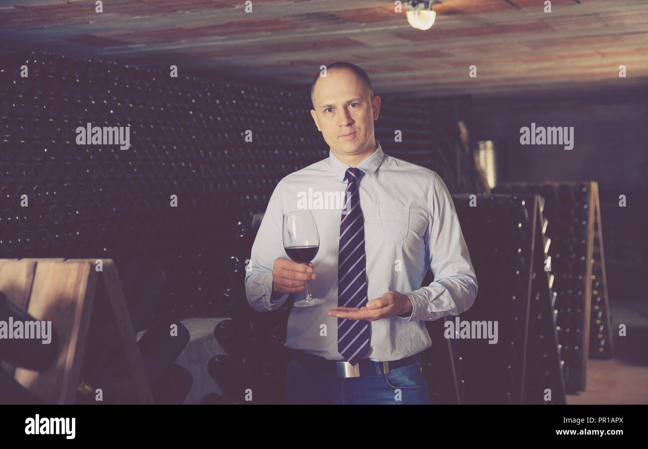 Confident winemaker inviting to wine cellar, offering glass of red wine ... Confident winemaker inviting to wine cellar, offering glass of red wine ...
