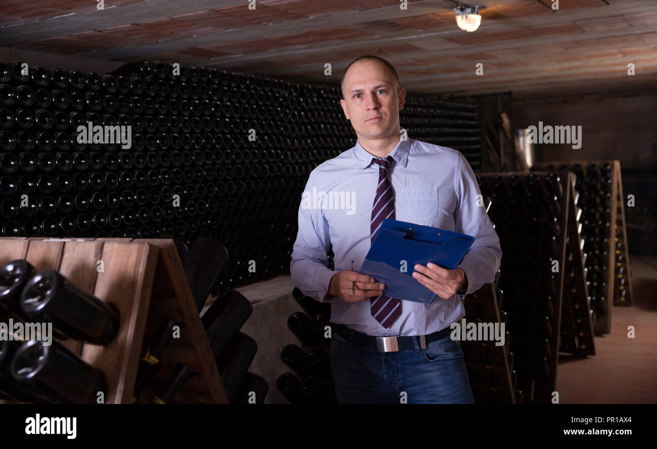 Confident male winemaker working in wine cellar, taking notes on ...