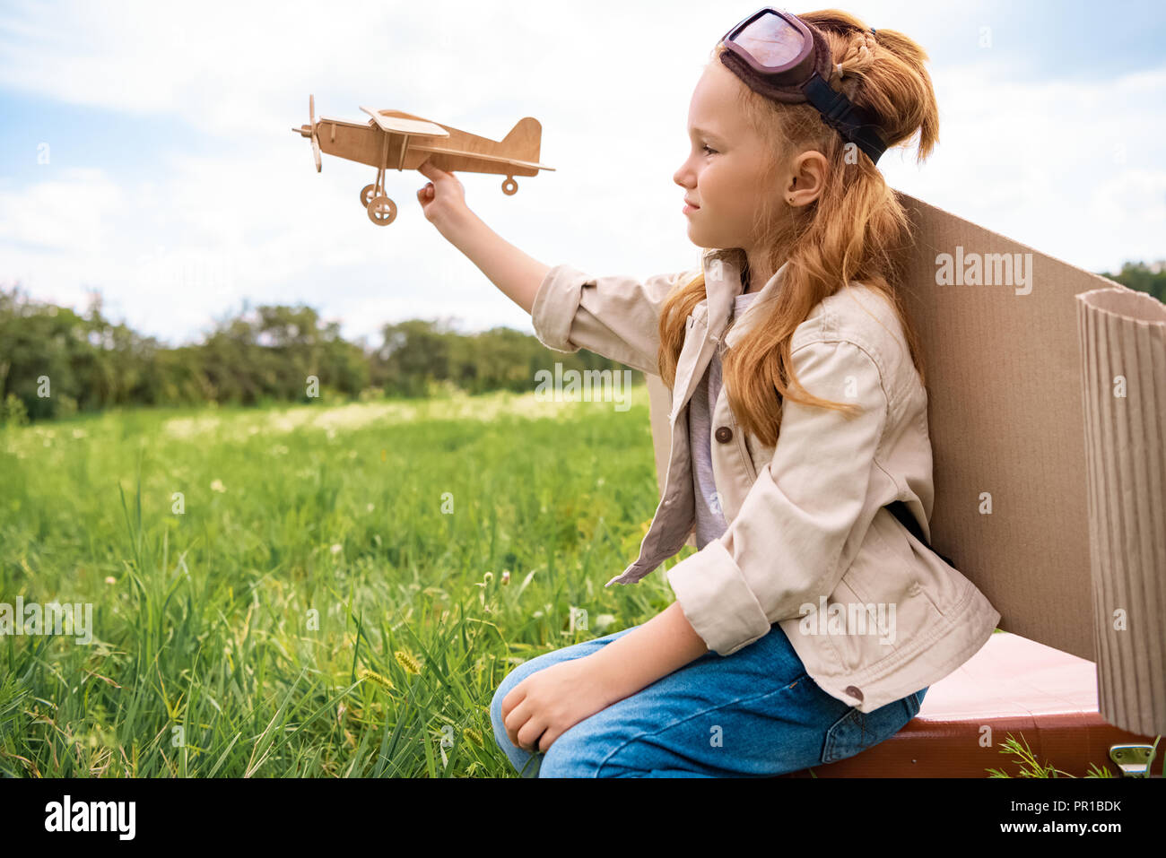 kid in pilot costume with wooden toy plane in hand sitting on retro ...