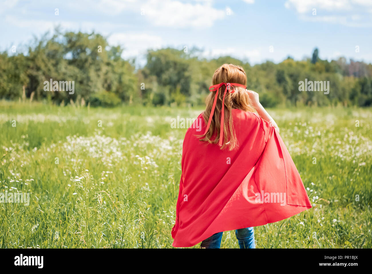 rear view of kid in red superhero cape and mask standing in summer ...