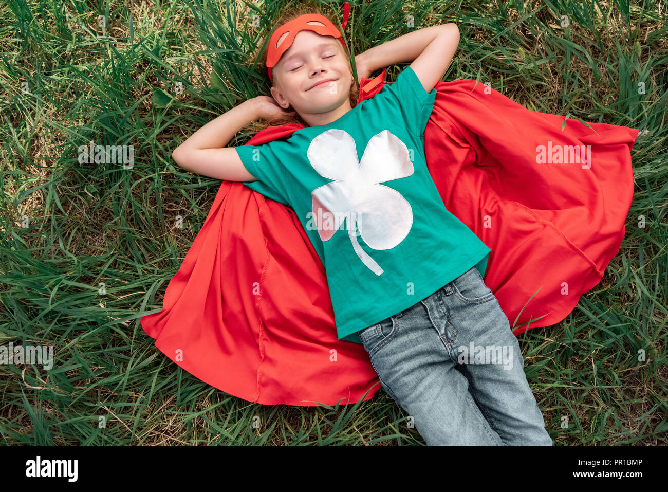 overhead view of kid with eyes closed in red superhero cape and mask ...