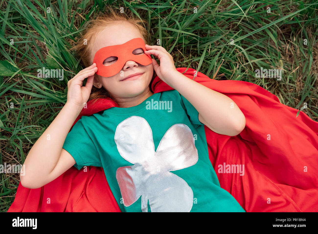 overhead view of kid with eyes closed in red superhero cape and mask ...