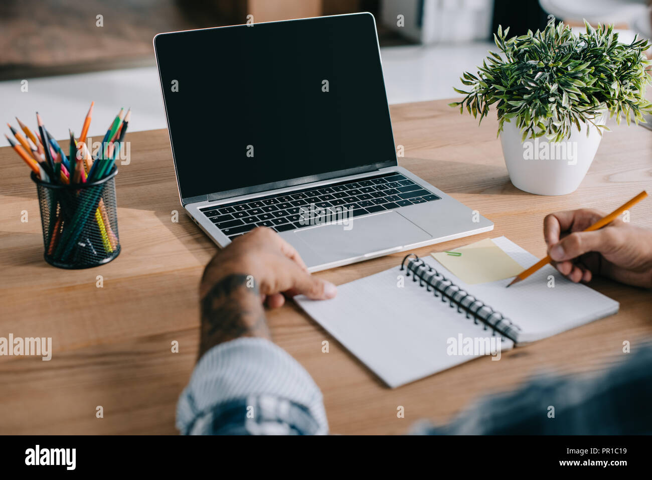 partial view of man writing in notebook at workplace with pencils and ...