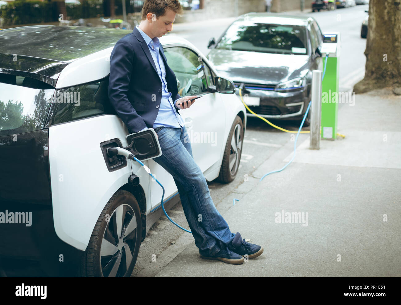 Businessman using mobile phone while charging electric car Stock Photo ...