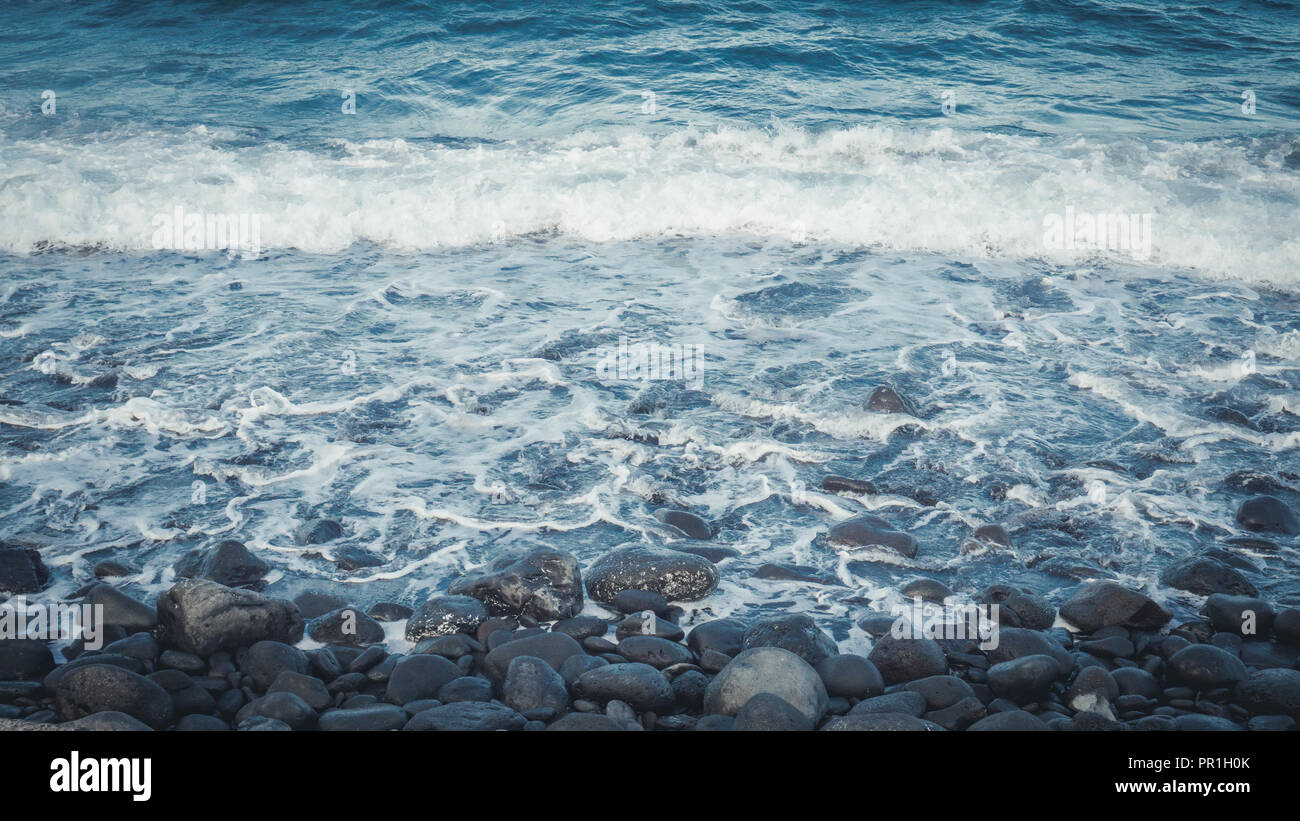 ocean shore, blue ocean waves, dark sand and black stones Stock Photo ...
