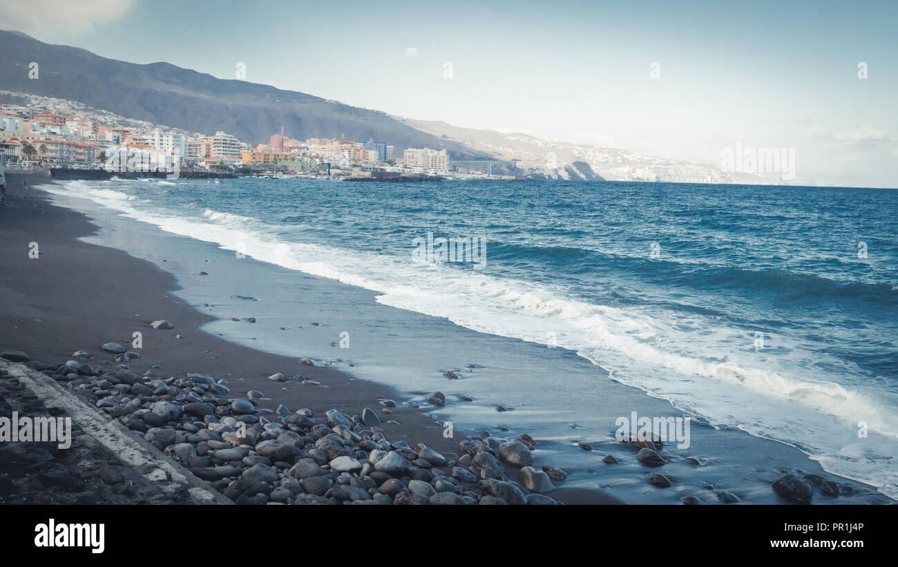 ocean shore, blue ocean waves, dark sand and black stones Stock Photo ...