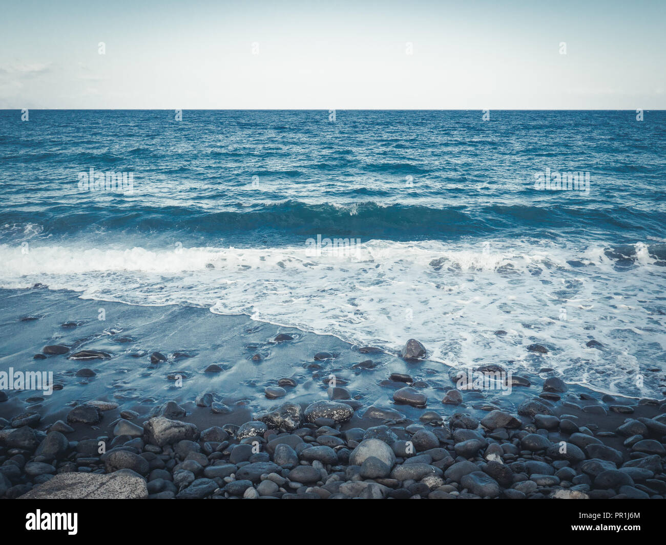 ocean shore, blue ocean waves, dark sand and black stones Stock Photo ...