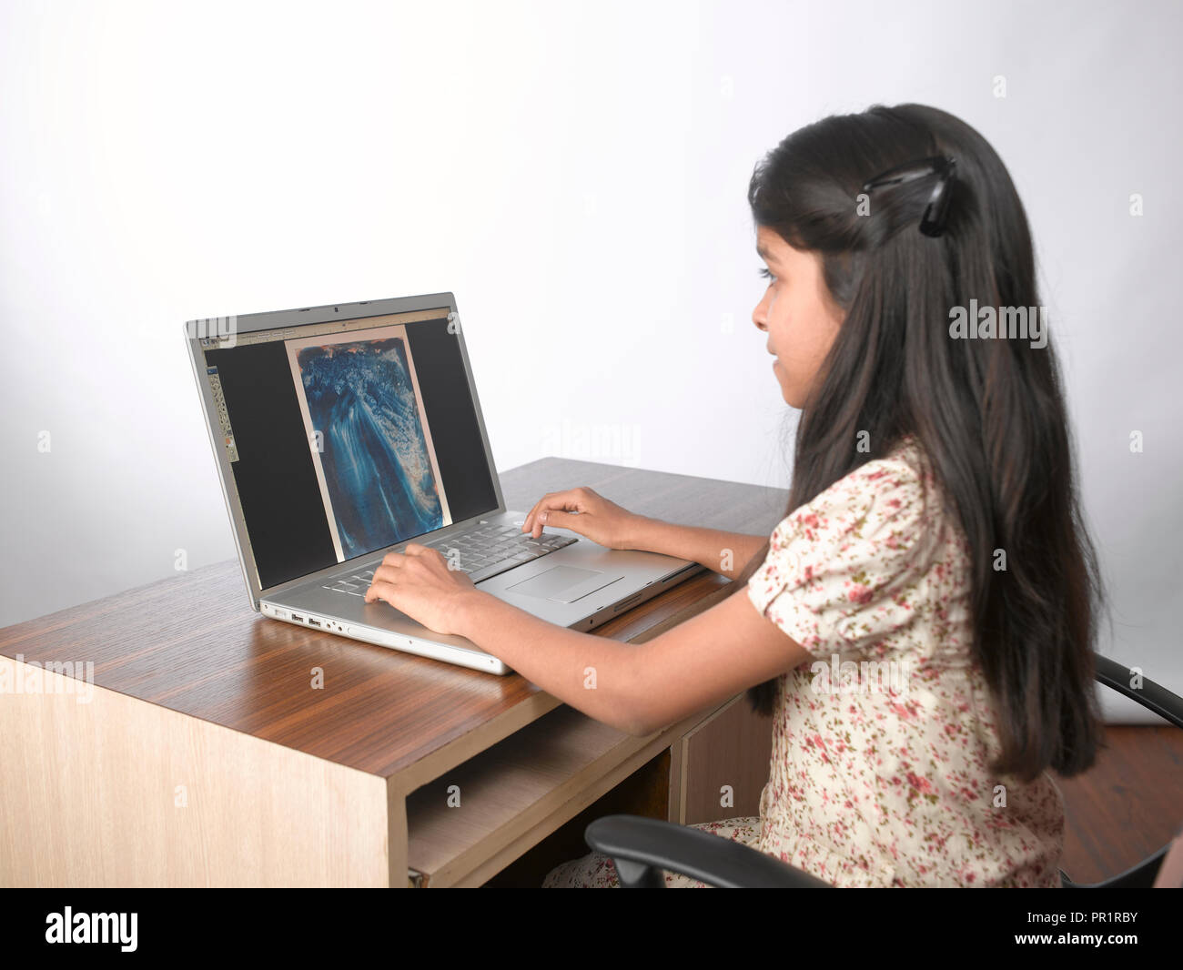 YOUNG GIRL WORKING ON A LAPTOP COMPUTER. SHOT AGAINST A PLAIN ...
