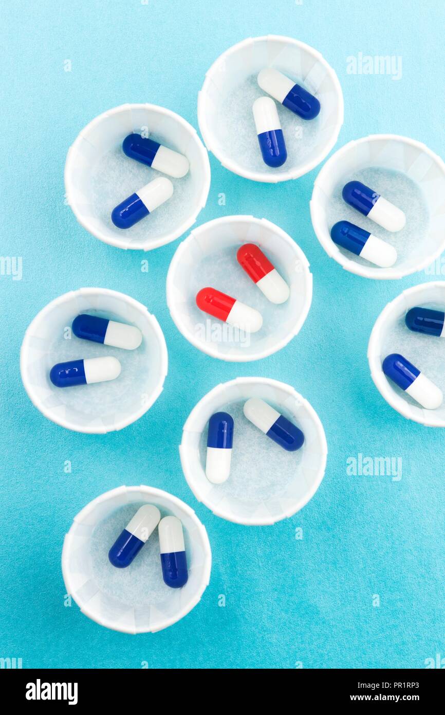 Paper medicine pots with blue and white capsules and a single dose of ...