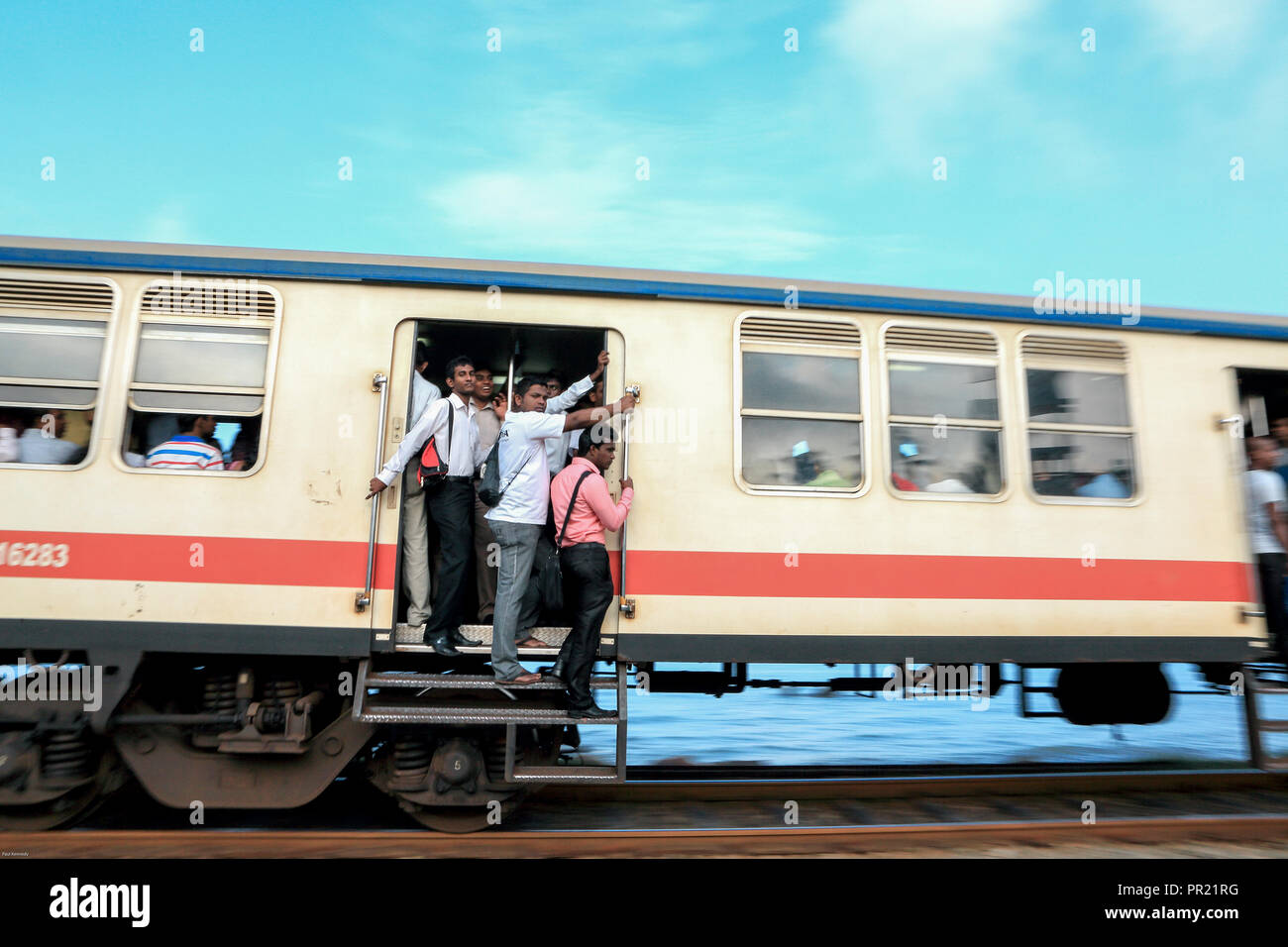 Sri Lankan businessmen riding in open doorway of commuter train in ...