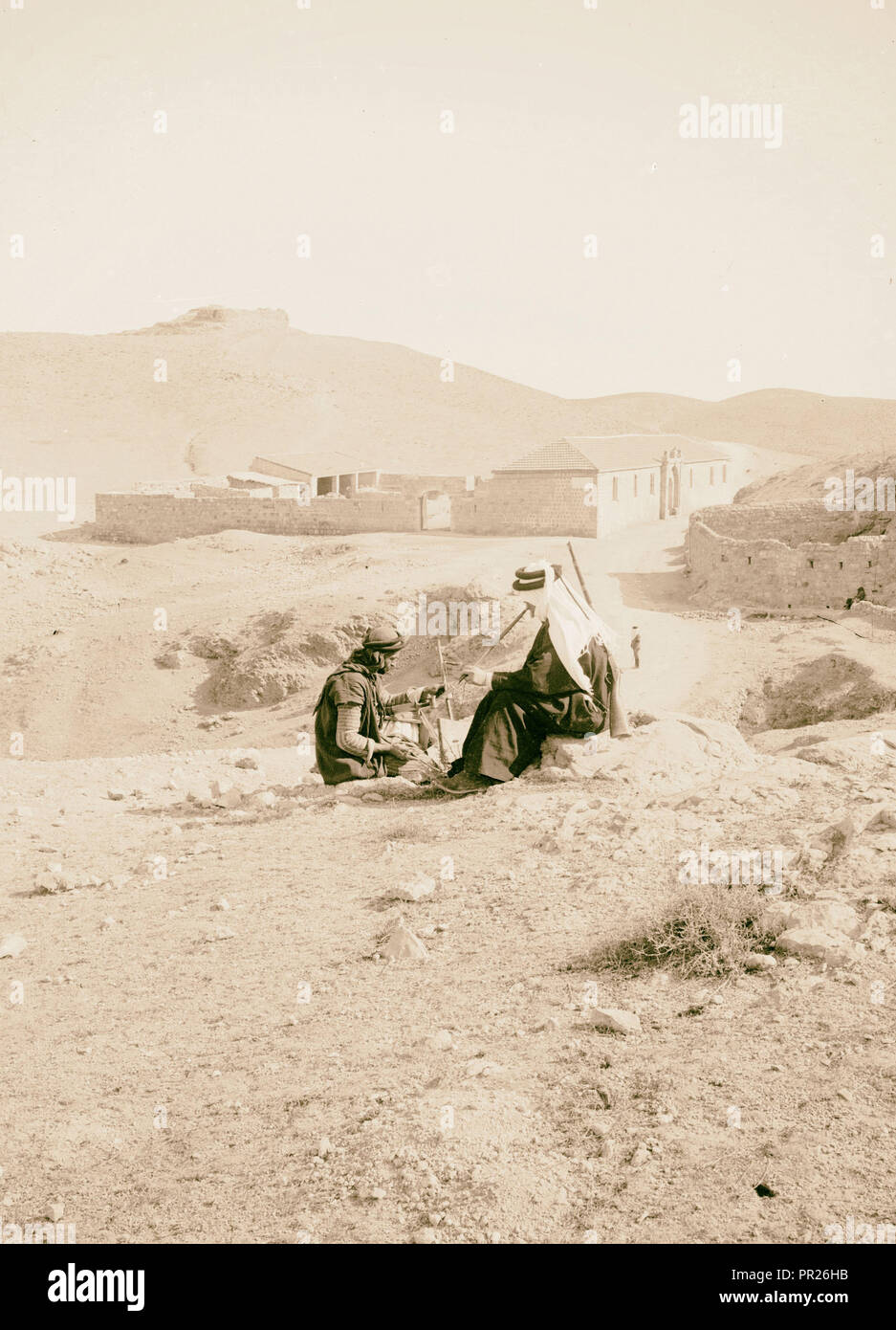 Two men seated in front of building, one with rababeh, a single string ...
