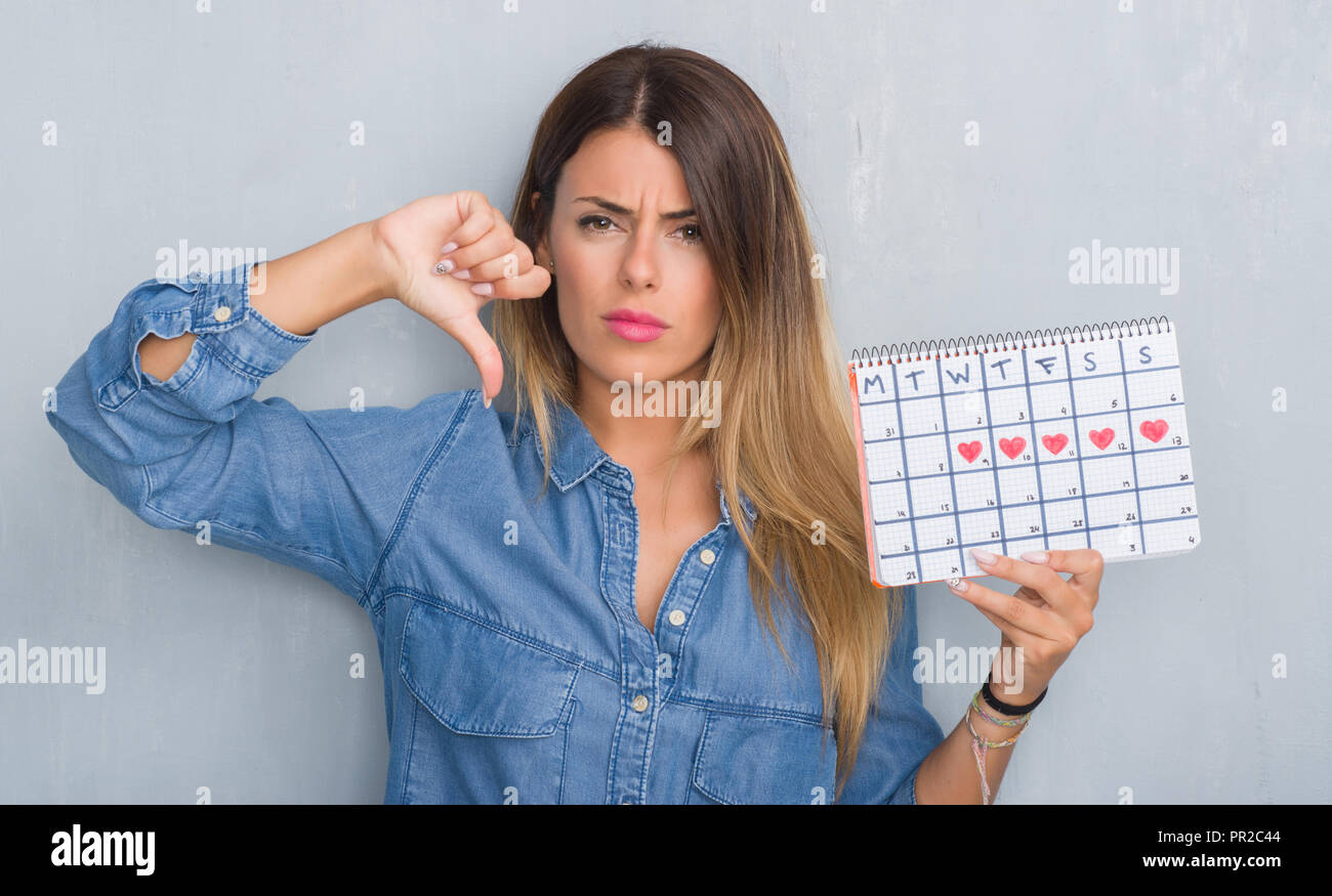 Young adult woman over grey grunge wall showing period calendar with ...