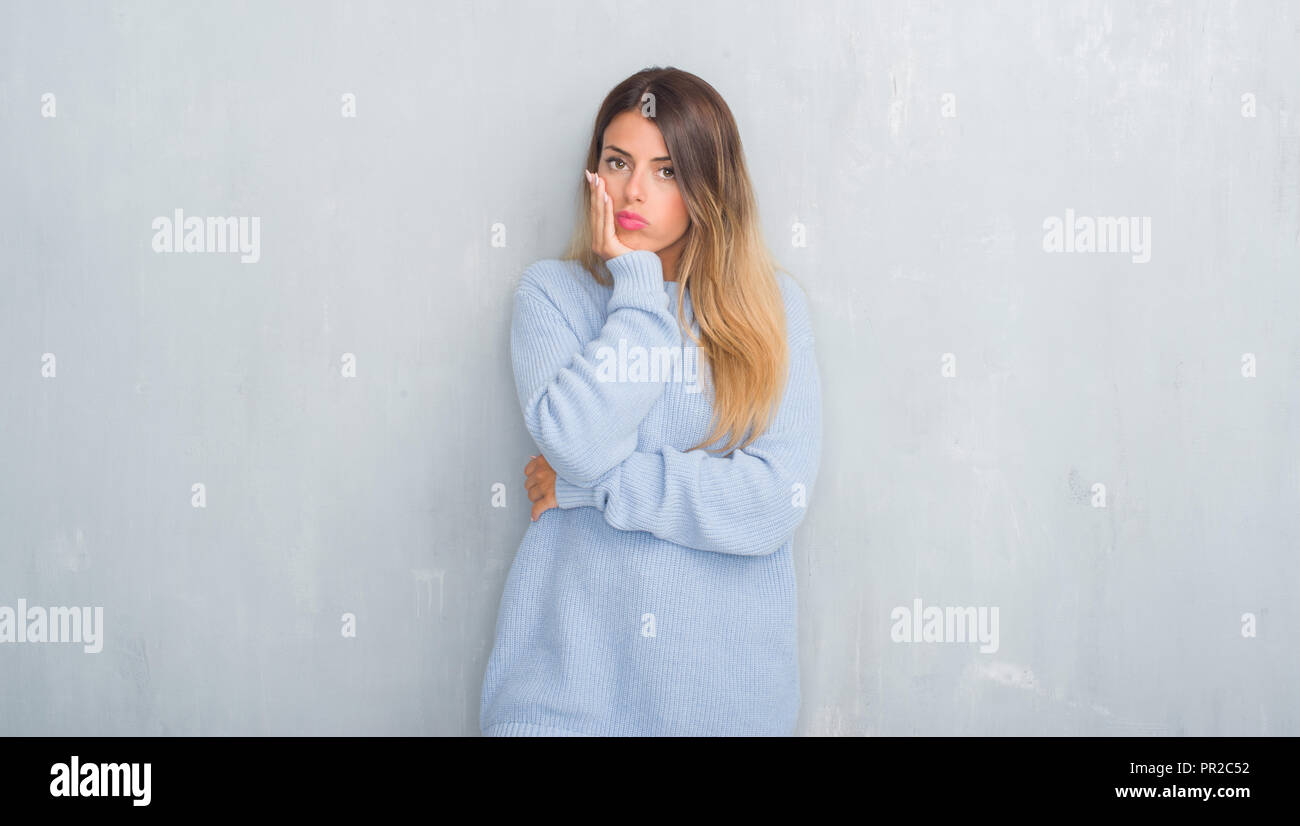 Young adult woman over grey grunge wall wearing winter outfit thinking ...