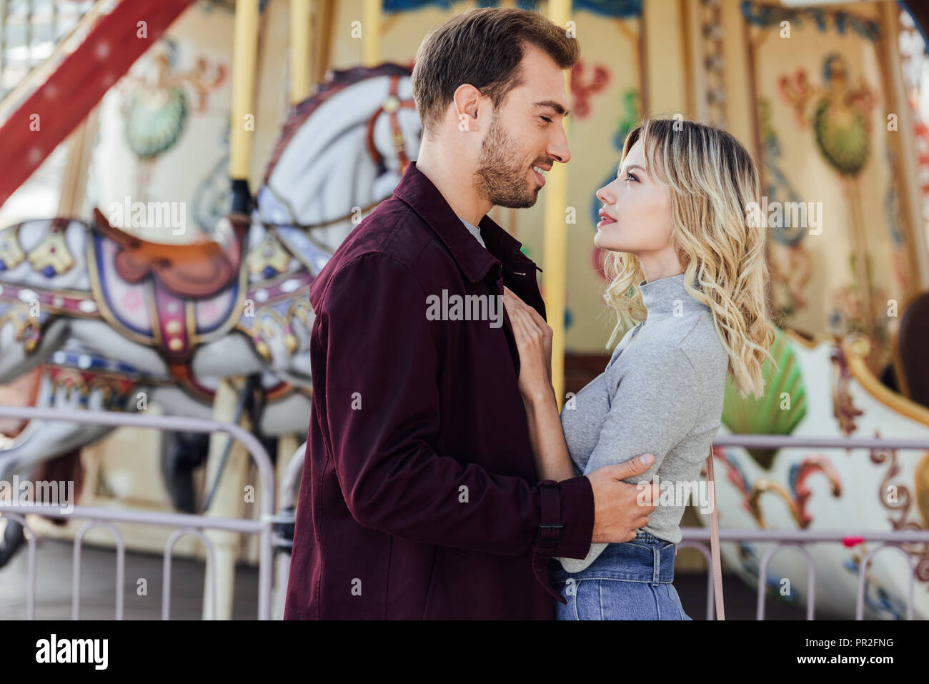 side view of romantic couple in autumn outfit cuddling near carousel in ...