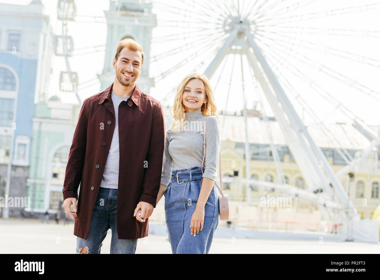 happy couple in autumn outfit holding hands and standing near ...