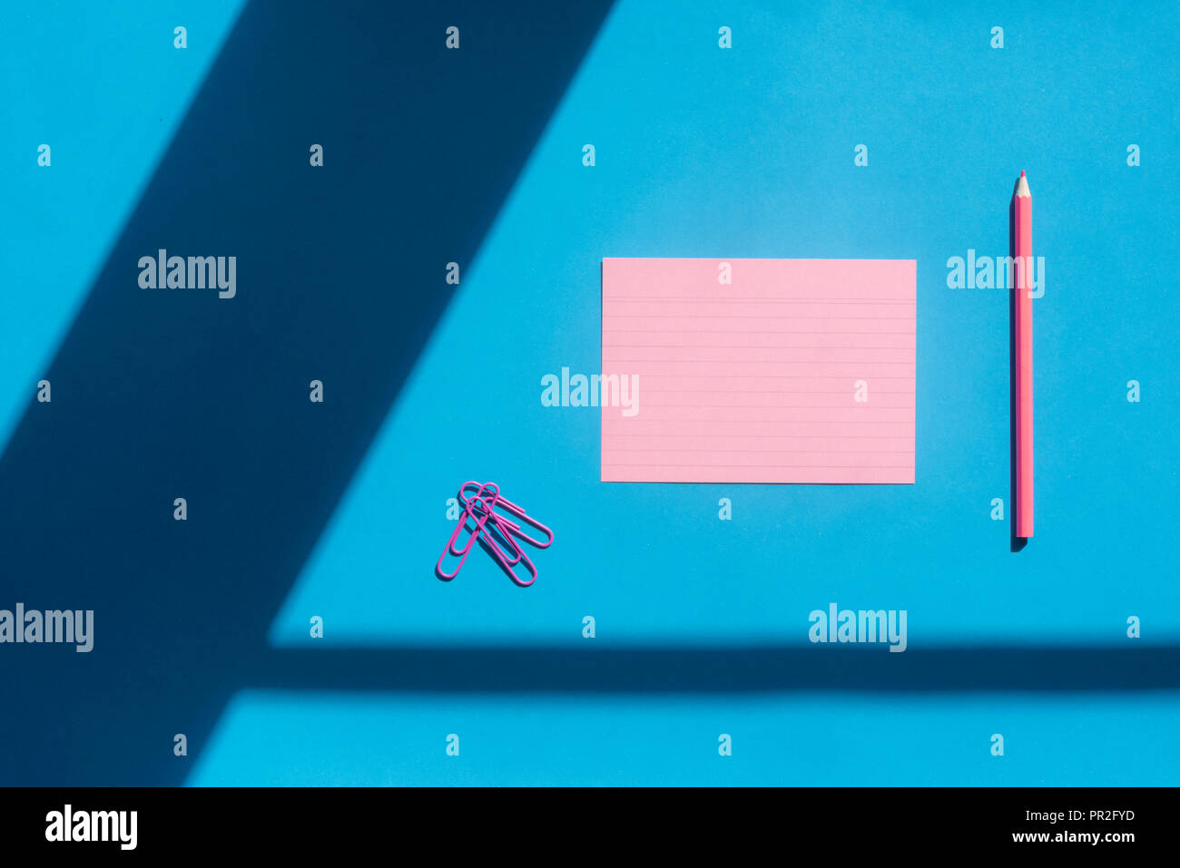 Minimalism concept with pink paper note, pencil and paper clips on blue ...
