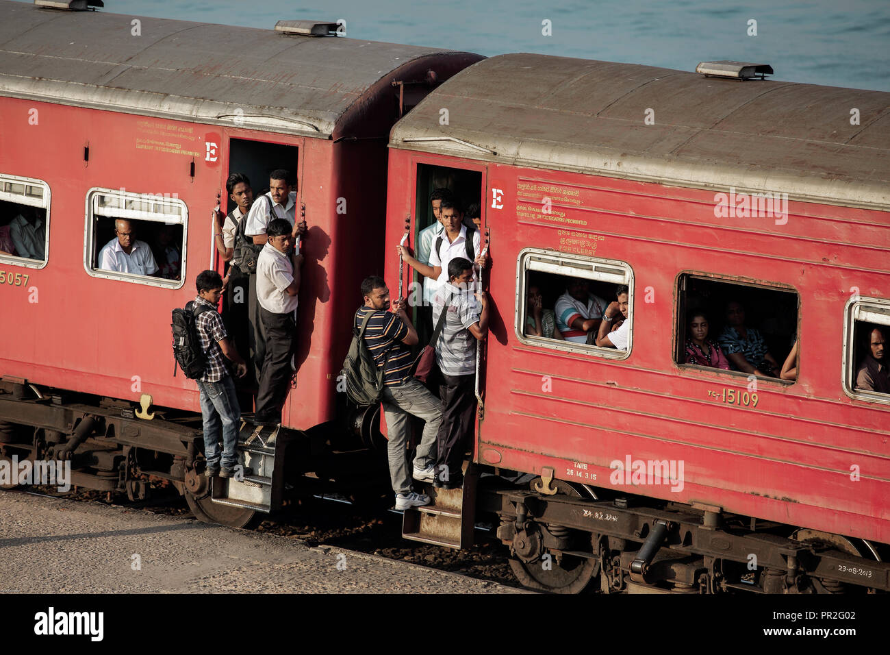 Passengers hanging out of doors on crowded commuter train at ...