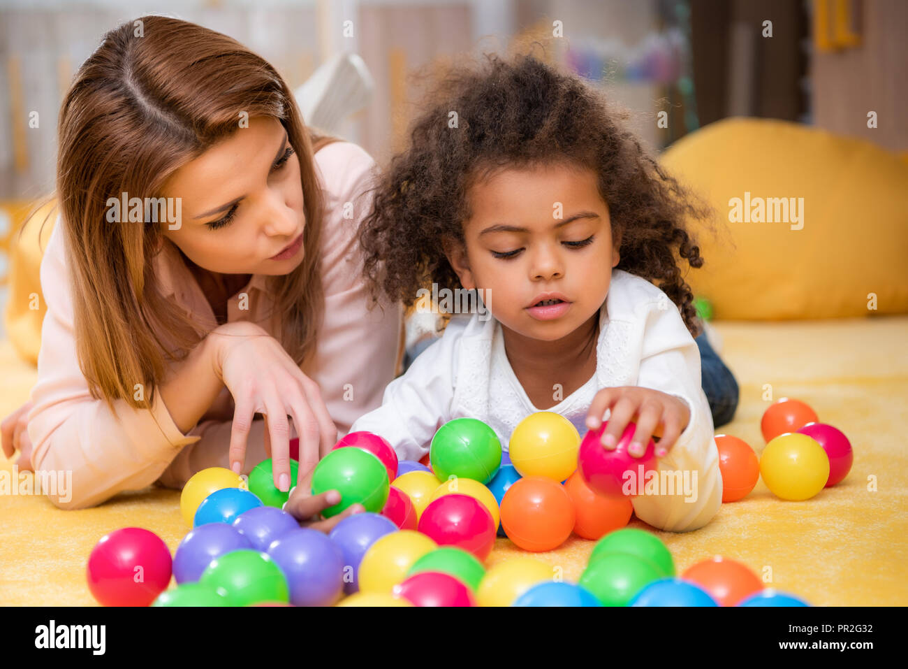 tutor and adorable african american child playing with colorful balls ...