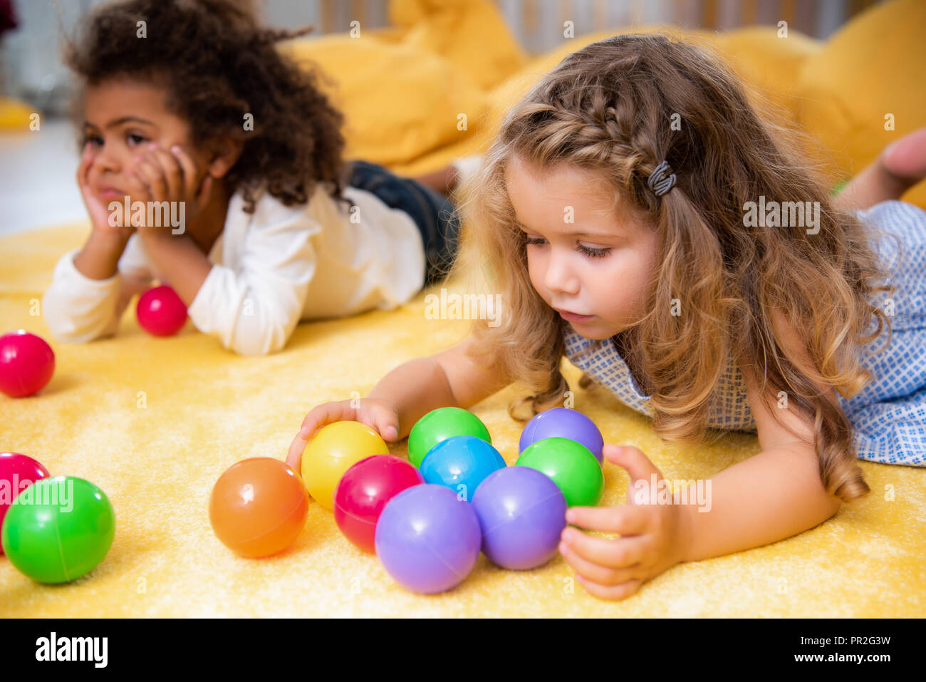 adorable multiethnic kids playing on yellow carpet with colored balls ...