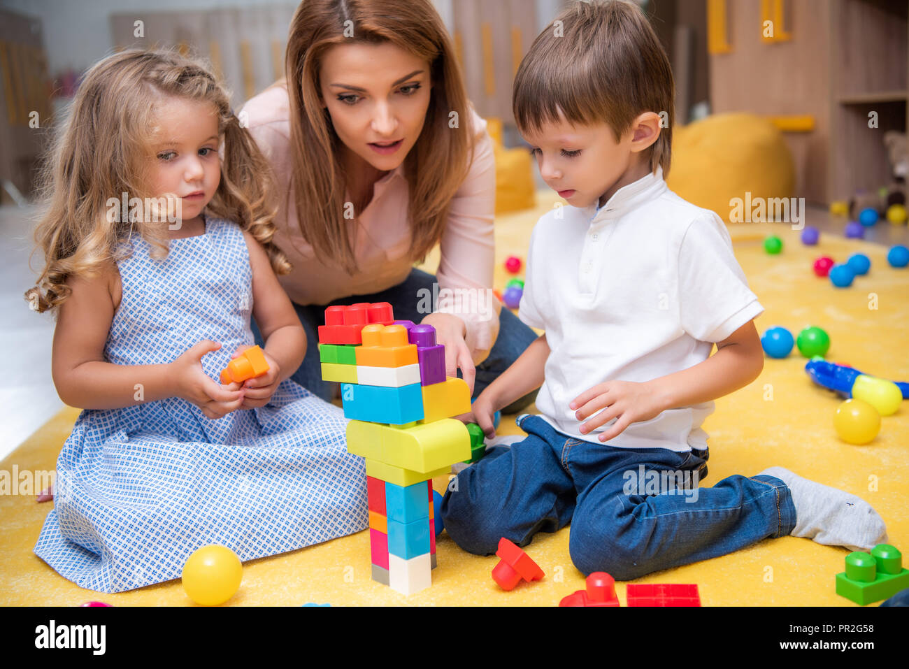 educator and adorable kids playing with constructor in kindergarten ...
