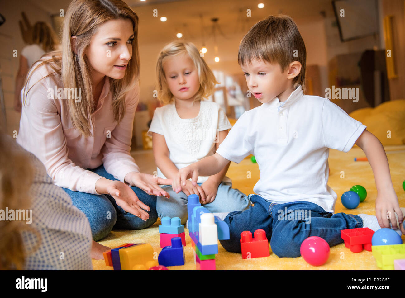 educator and caucasian kids playing with constructor in kindergarten ...