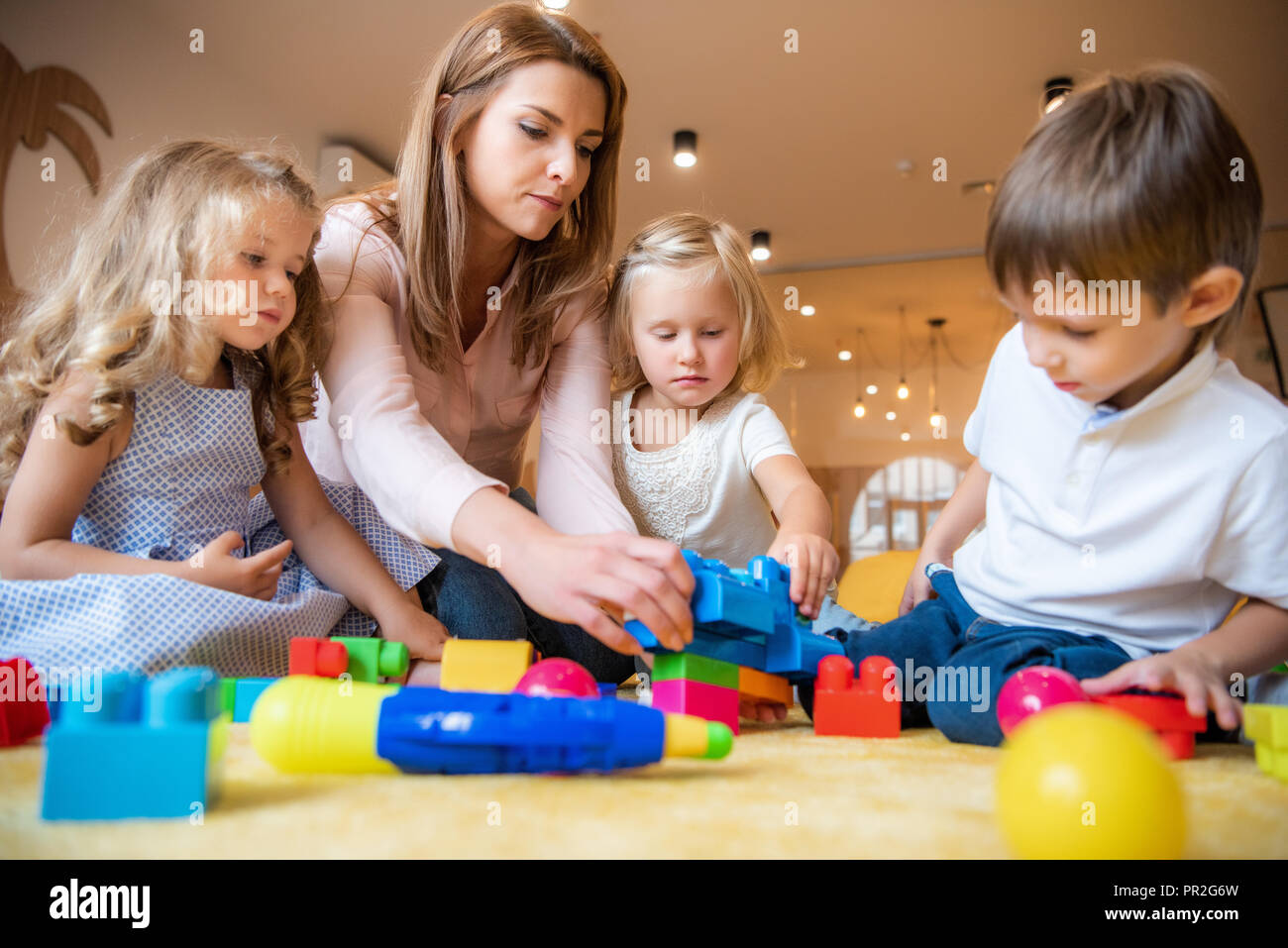 educator and adorable kids playing with constructor in kindergarten ...