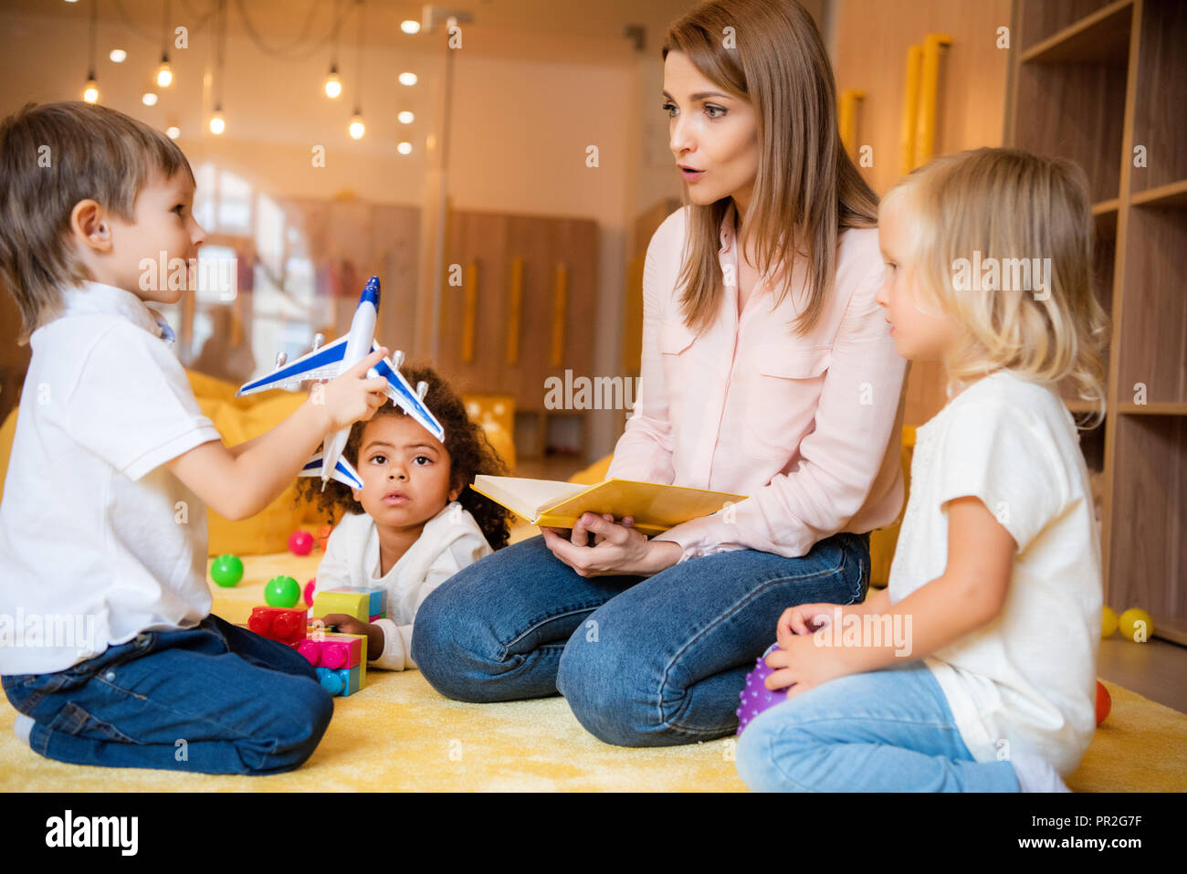 educator reading book for multiethnic kids in kindergarten Stock Photo ...