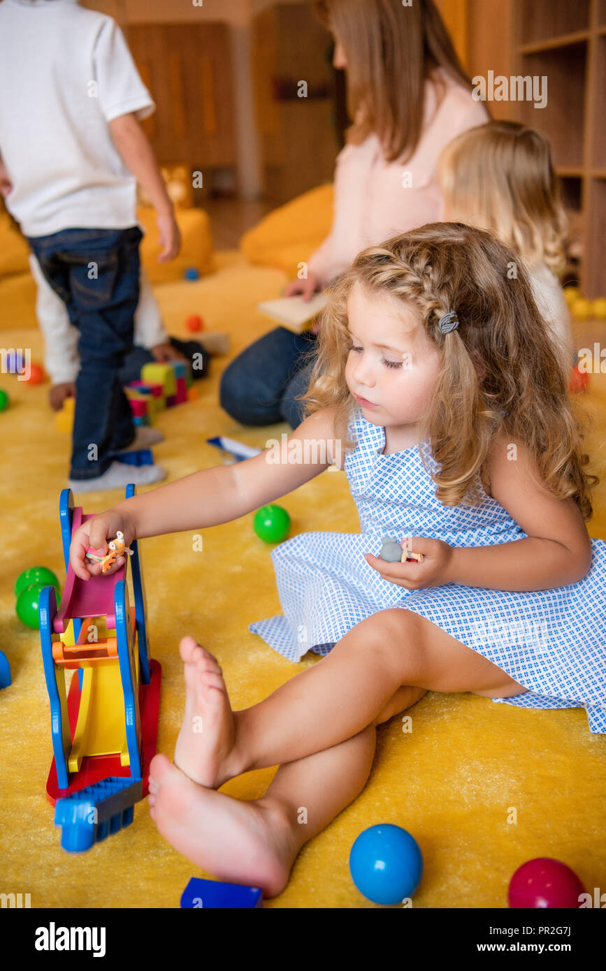 adorable kid in dress sitting on carpet and playing with toys in ...