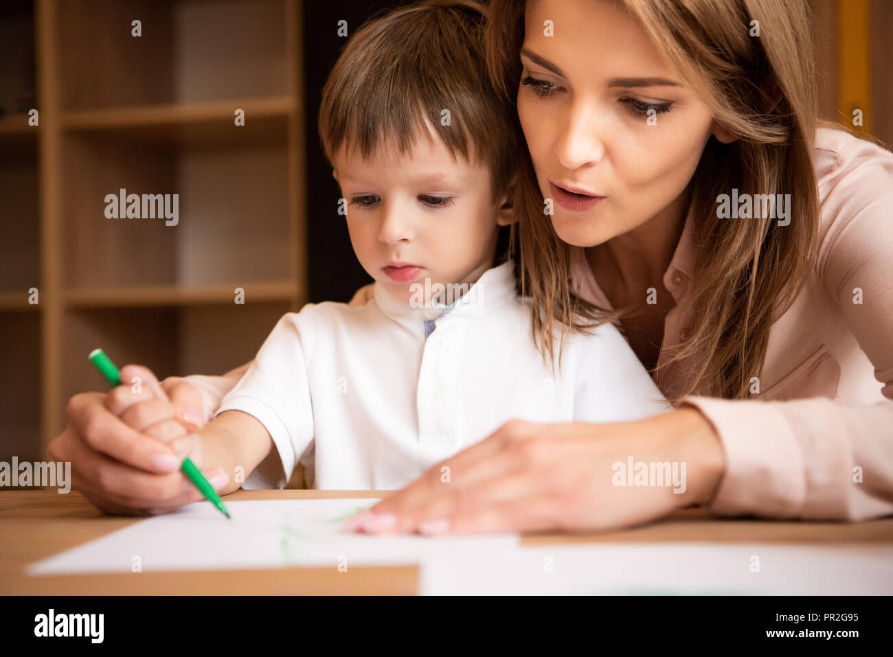 educator helping boy drawing with green felt pen in kindergarten Stock ...