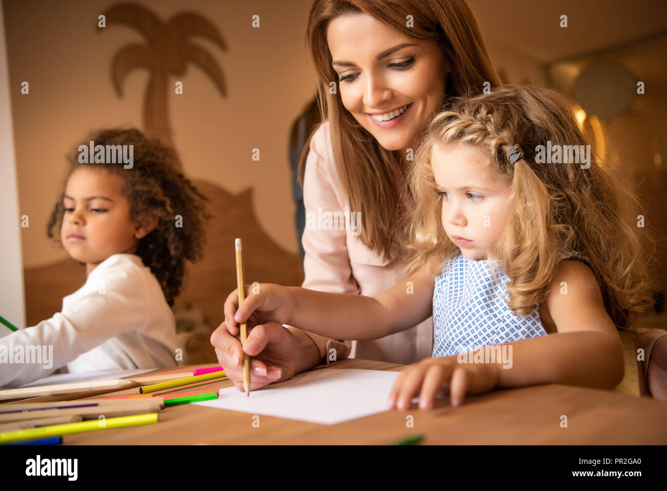happy tutor helping kid drawing in kindergarten Stock Photo - Alamy