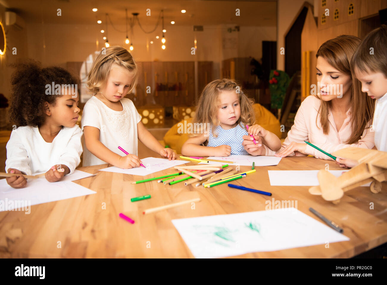 educator drawing together with multicultural kids in kindergarten Stock ...