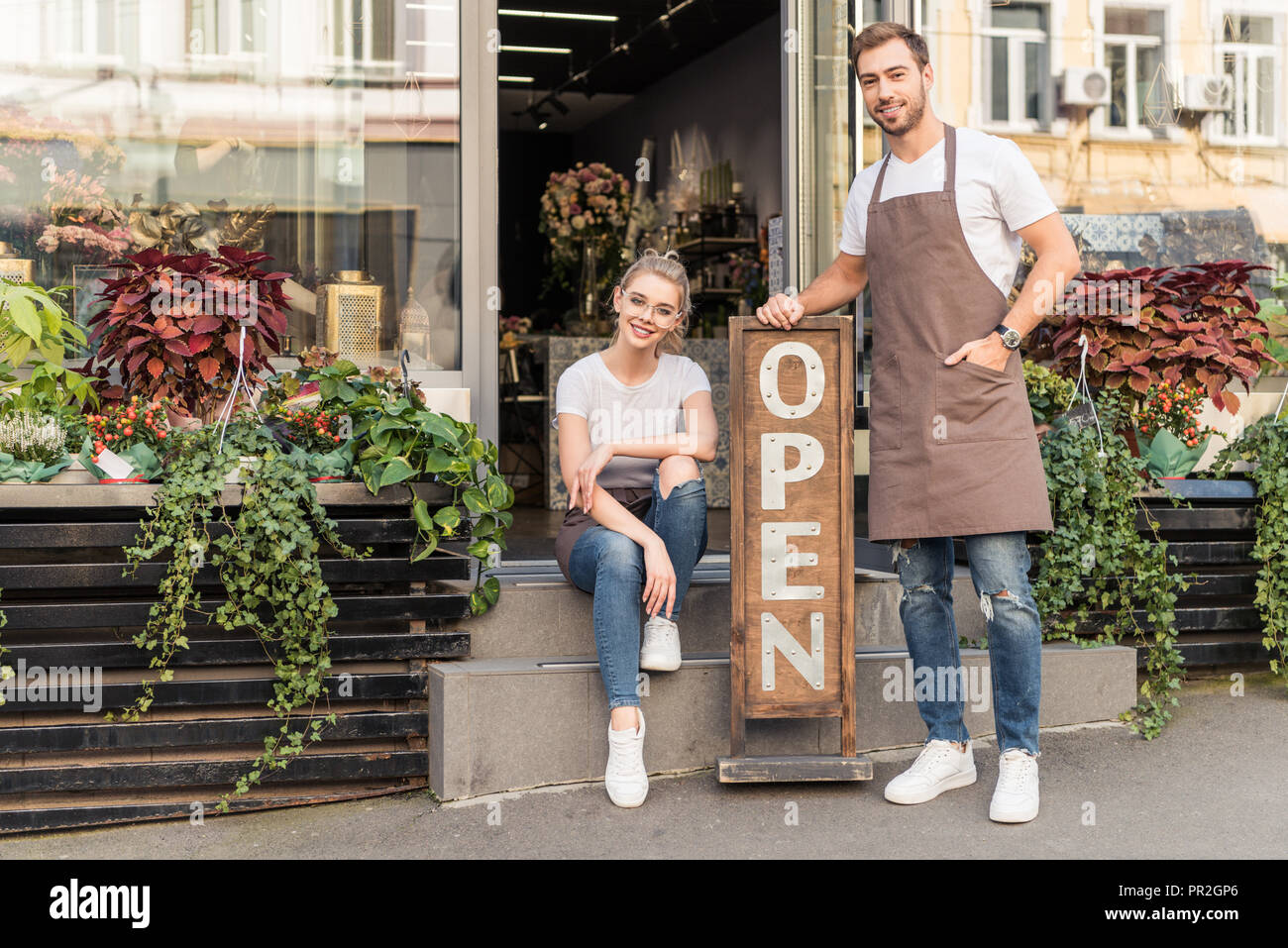 smiling flower shop owners looking at camera on street with open ...