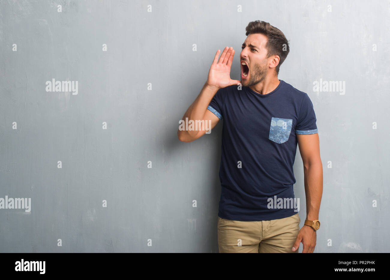 Handsome young man over grey grunge wall shouting and screaming loud to ...